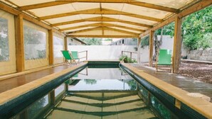 Piscina interior com estrutura de telhado de madeira, paredes de vidro transparente e piso revestido de azulejos.