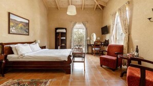 Quarto com cama de madeira, uma cadeira, uma mesa pequena e televisão na parede.