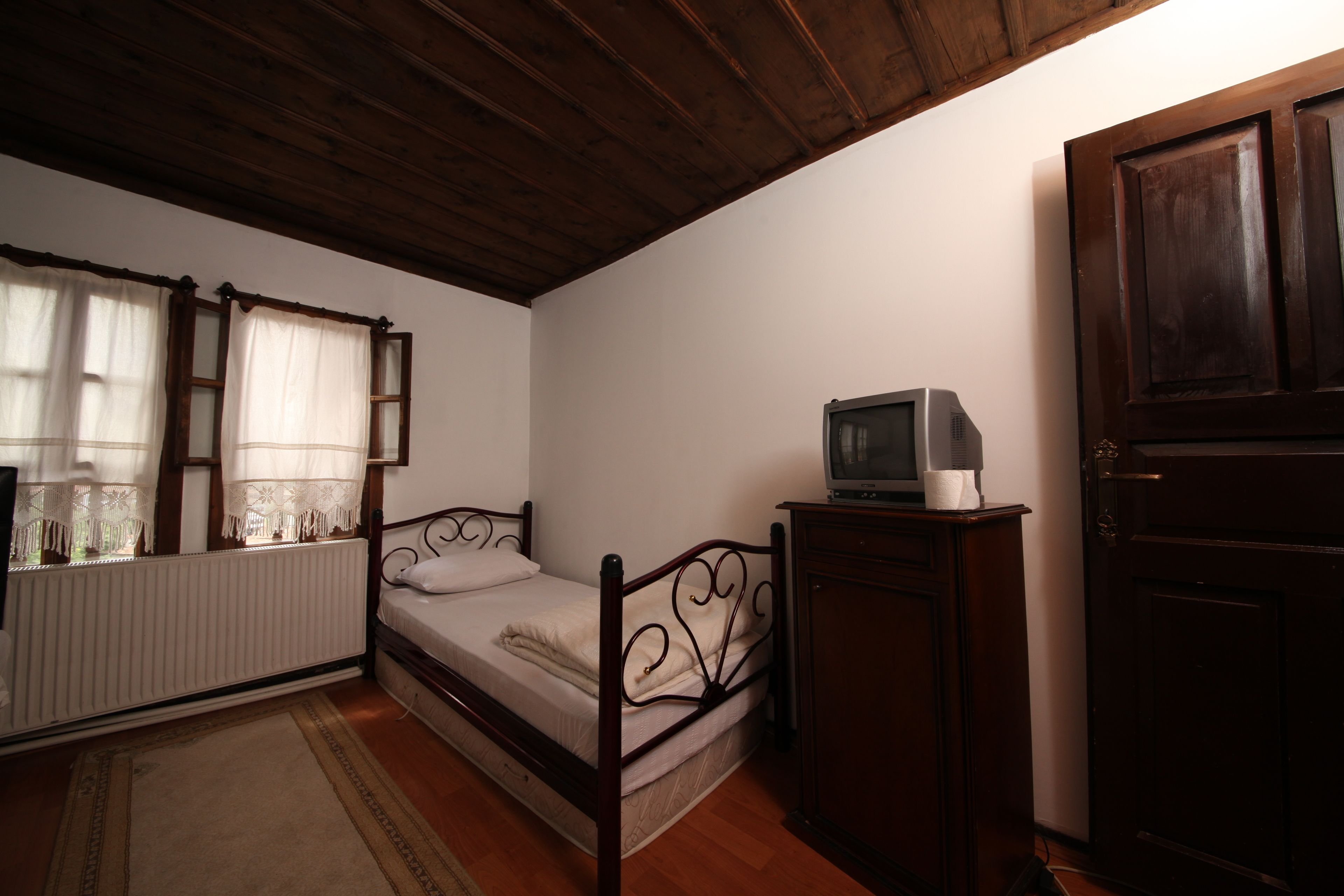 Quarto com teto de madeira, cama com estrutura de metal, televisão sobre uma mesinha e um guarda-roupa.