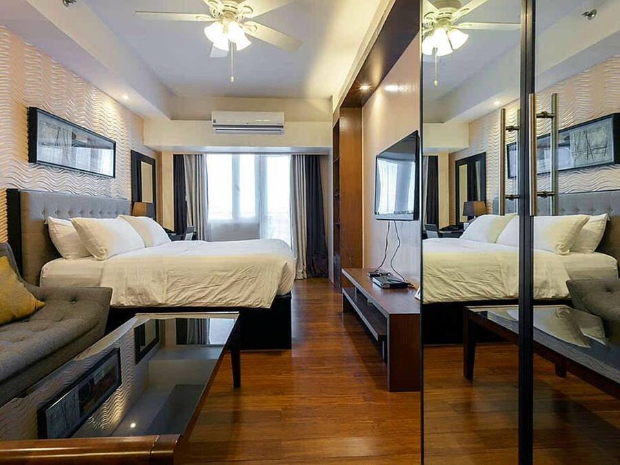Quarto de hotel com duas camas, um sofá, uma TV e um ventilador de teto.