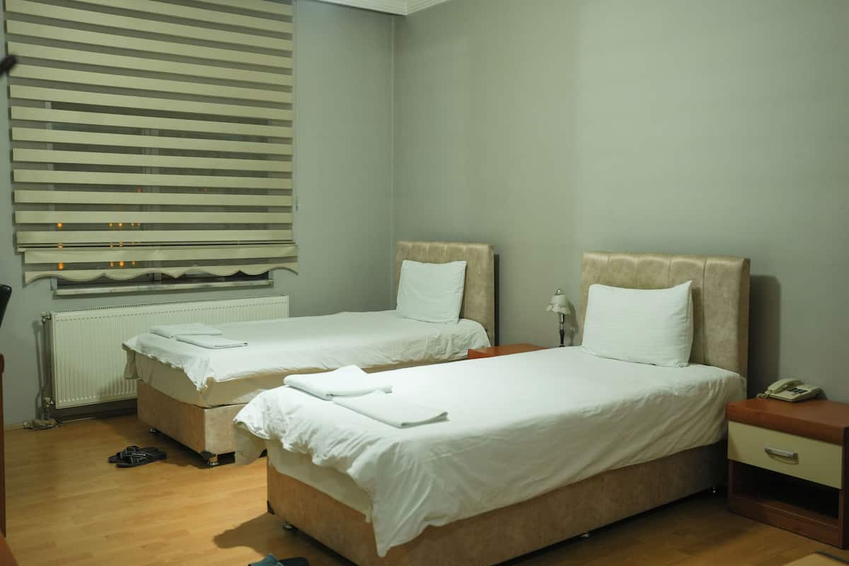 Quarto com duas camas, um radiador, mesa de cabeceira com abajur e telefone.