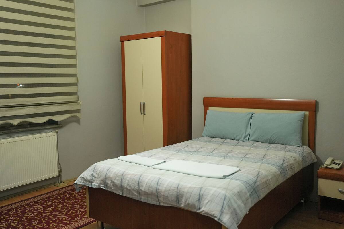 Quarto com cama, guarda-roupa, radiador e mesa de cabeceira com telefone.