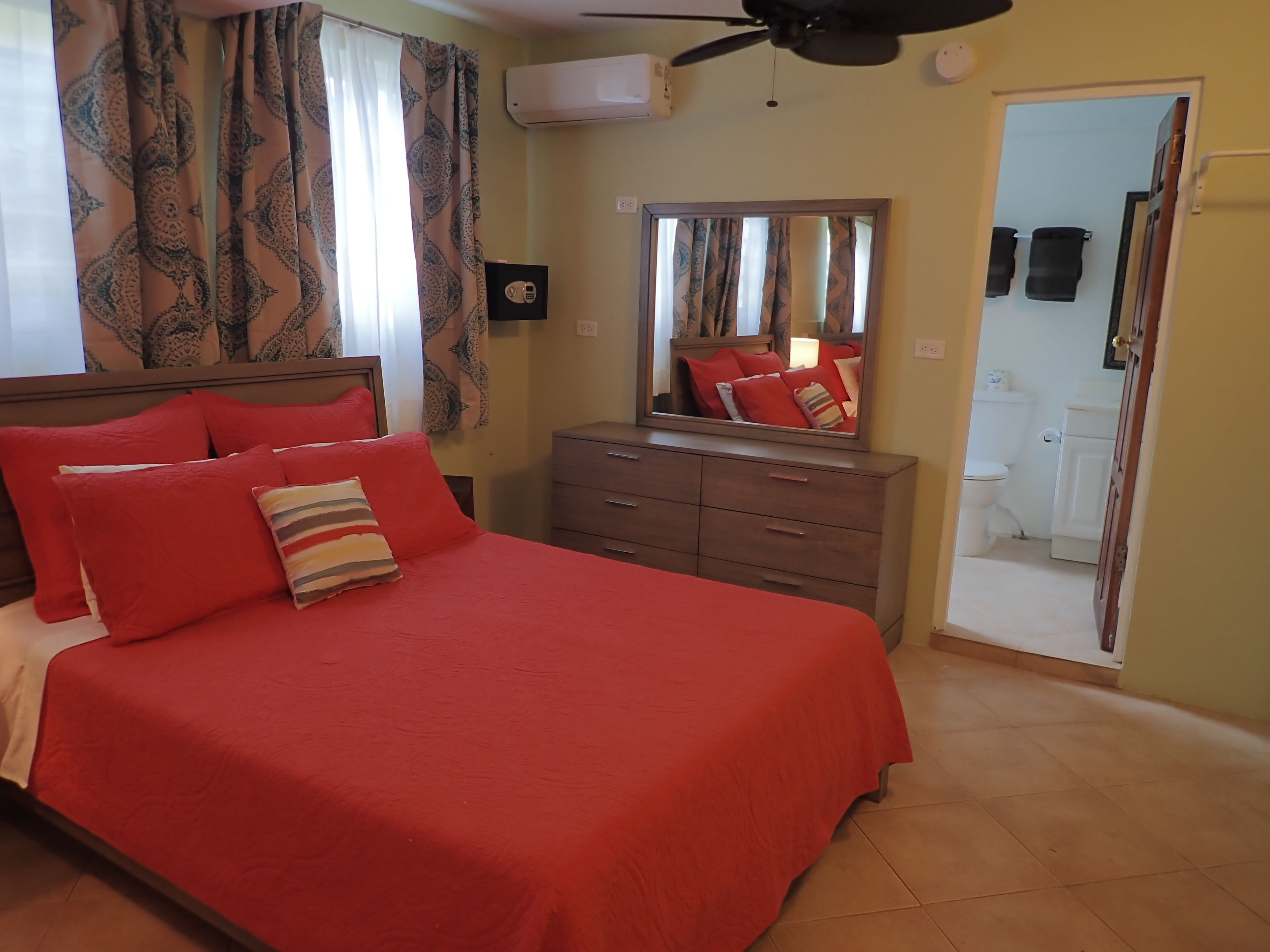 Quarto com cama, cômoda, espelho e porta para um banheiro.