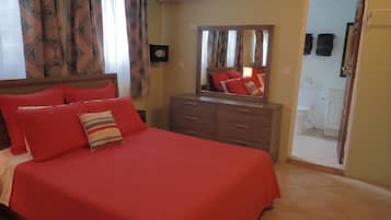 Quarto com cama, cômoda, espelho e porta para um banheiro.