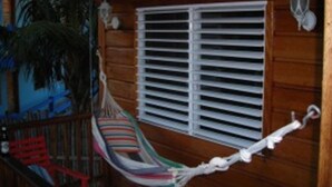 Uma cabana de madeira com uma rede, uma janela com persianas e um candeeiro.