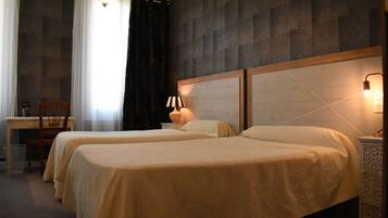 Quarto de hotel com duas camas, uma mesa, uma cadeira e uma mesa de cabeceira com abajur.