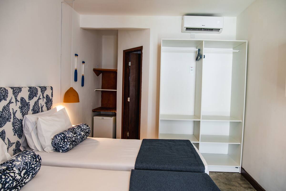Quarto de hotel com cama, guarda-roupa, secretária e ar condicionado.