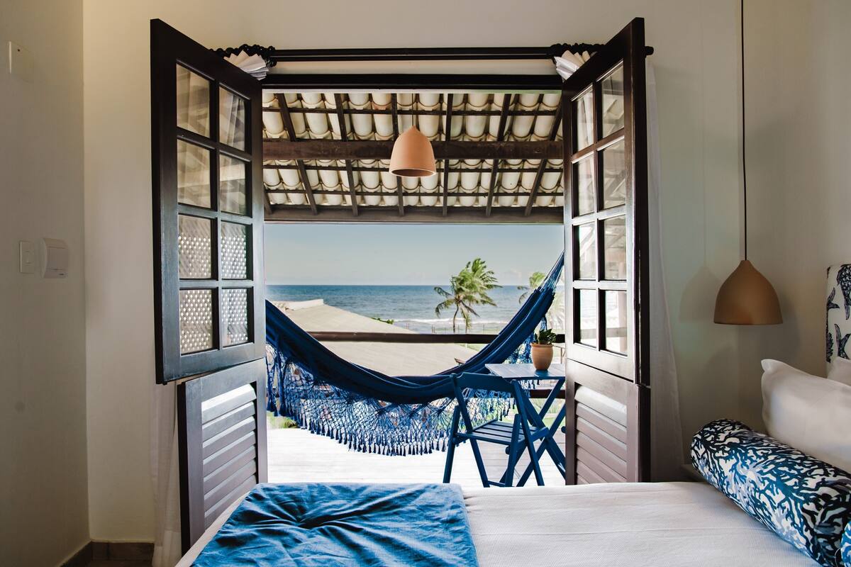 Quarto com vista para a praia, uma rede e uma cama com colcha azul.