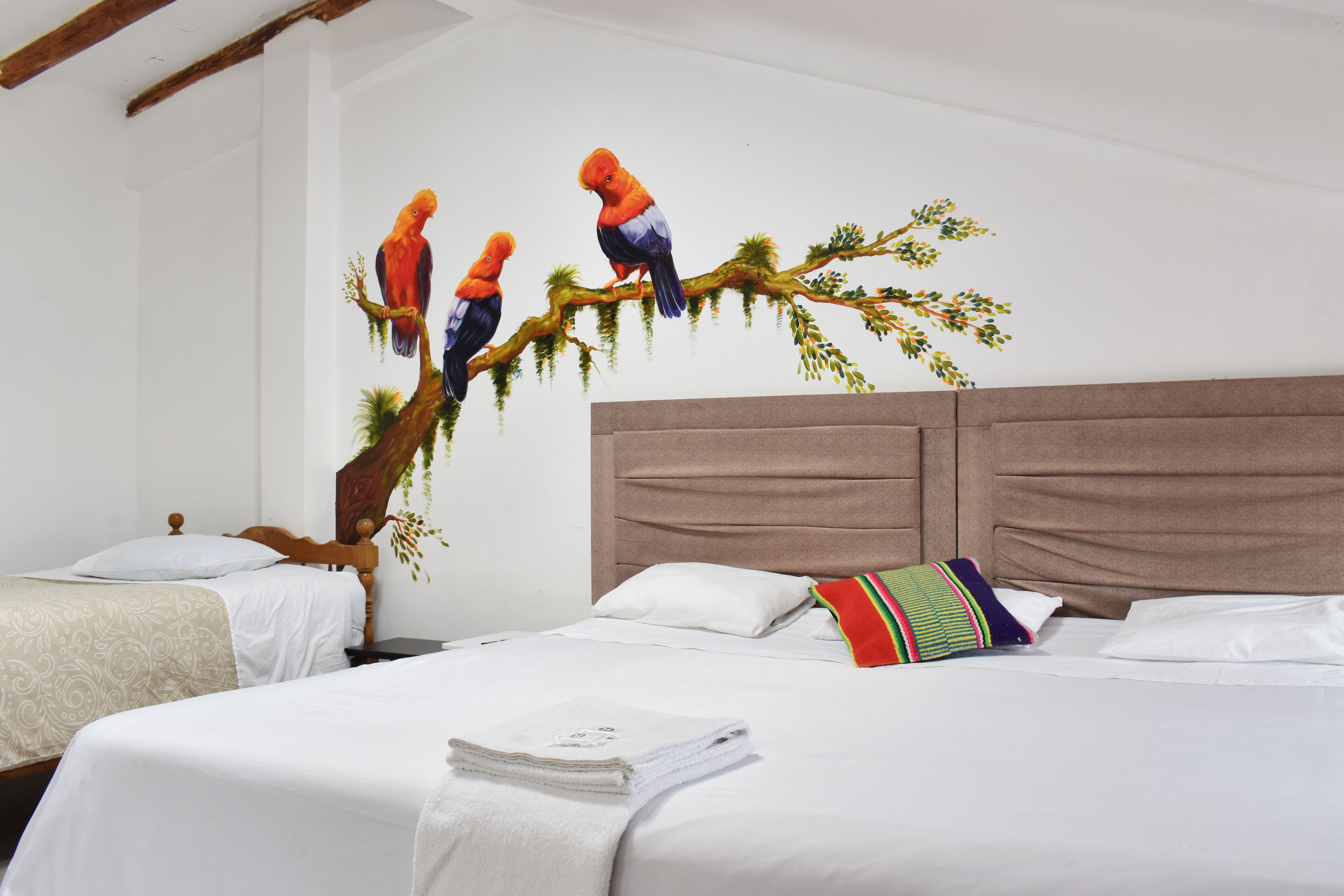 Quarto de hotel com duas camas, um mural de araras em uma árvore e cabeceira marrom.