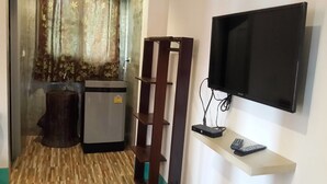 Quarto compacto com geladeira, escada de madeira, televisão de tela plana e prateleira com controle remoto.