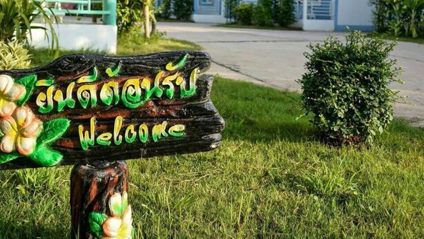 Uma placa de madeira com uma girafa e a palavra 'Welcome' em inglês, um edifício azul com teto branco e uma antena parabólica no teto.