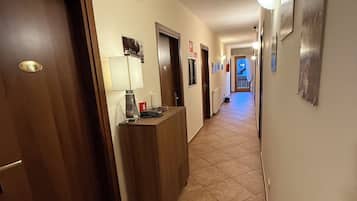 Corredor de hotel com balcão de recepção, porta com placa de número e acesso a outro quarto.