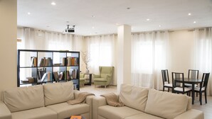 Uma sala de estar moderna com um sofá bege, uma mesa de centro, uma estante, uma poltrona verde e uma área de jantar com mesa e cadeiras.