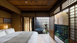 Quarto japonês tradicional com tatames, uma cama grande e vista para um jardim através de um painel shoji.
