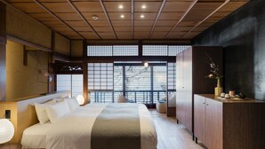 Quarto moderno com uma cama grande, piso de madeira e vista da cidade por grandes janelas.