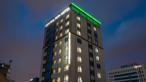 Um hotel alto com um letreiro que diz 'CENTRAL PARK HOTEL' e um detalhe verde no topo.