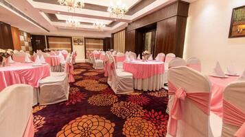 Uma sala de banquetes com mesas redondas, cadeiras adornadas com fitas cor-de-rosa e um tapete floral.
