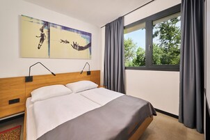 Quarto de hotel moderno com uma cama grande, cabeceira com telefone, janela com cortinas e um quadro na parede.