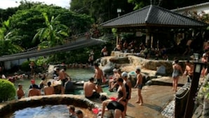 Uma onsen japonesa tradicional com várias piscinas termais, bancos de pedra e um pavilhão coberto.
