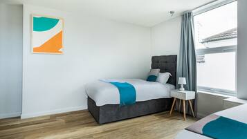 Quarto moderno com cama, mesa de cabeceira e janela com cortinas.