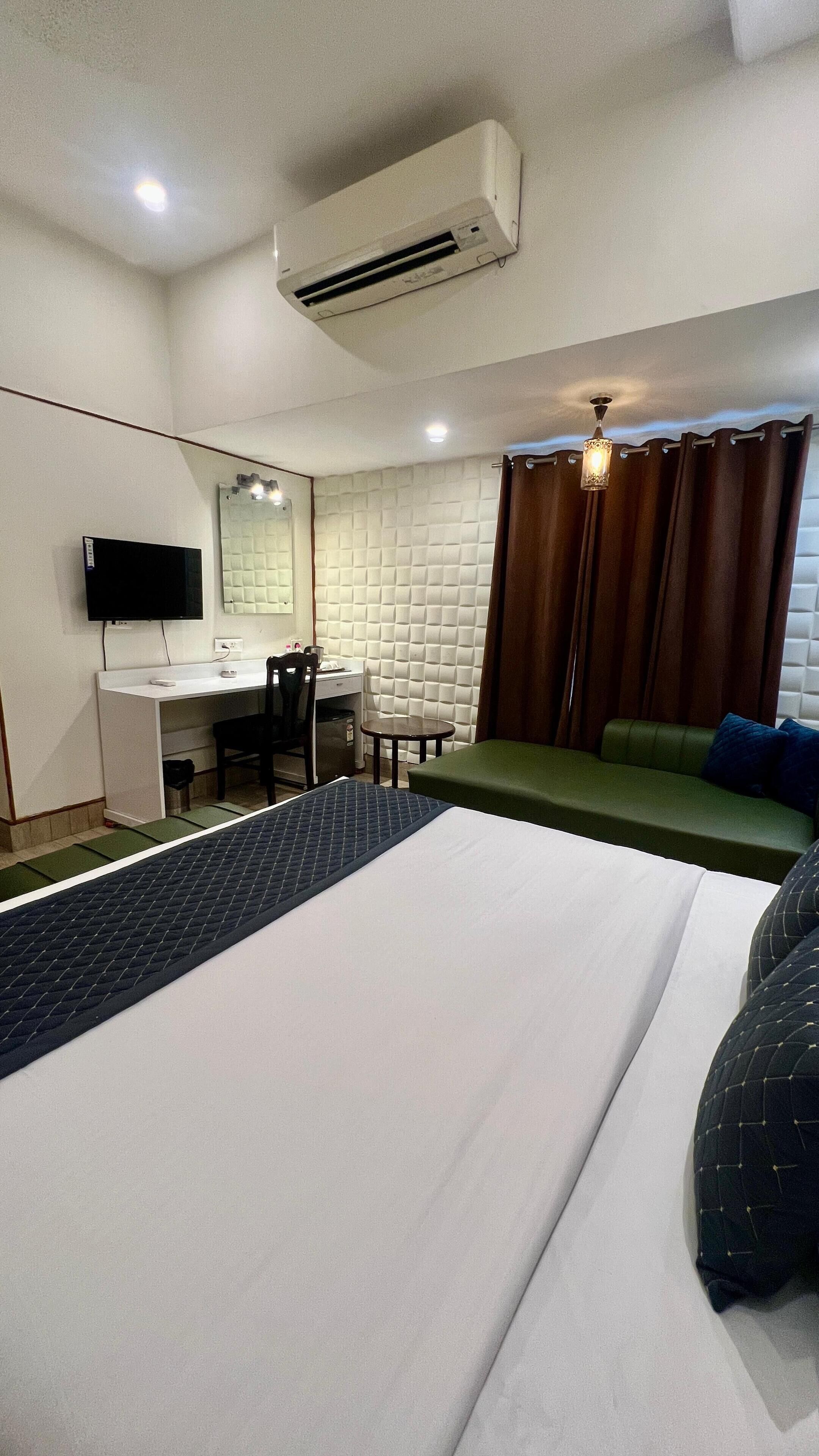 Quarto de hotel com cama, escrivaninha, cadeira, mesa pequena, televisão e janela com cortinas.