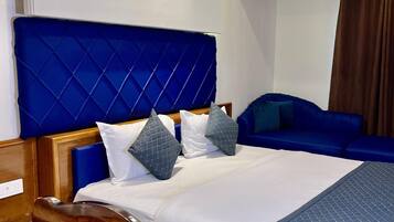 Quarto de hotel com uma cama grande, cabeceira de madeira, sofá azul estofado e ar condicionado branco na parede.