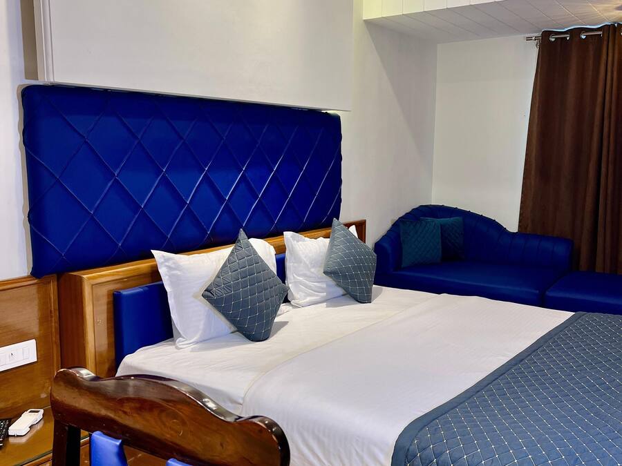 Quarto de hotel com uma cama grande, cabeceira de madeira, sofá azul estofado e ar condicionado branco na parede.