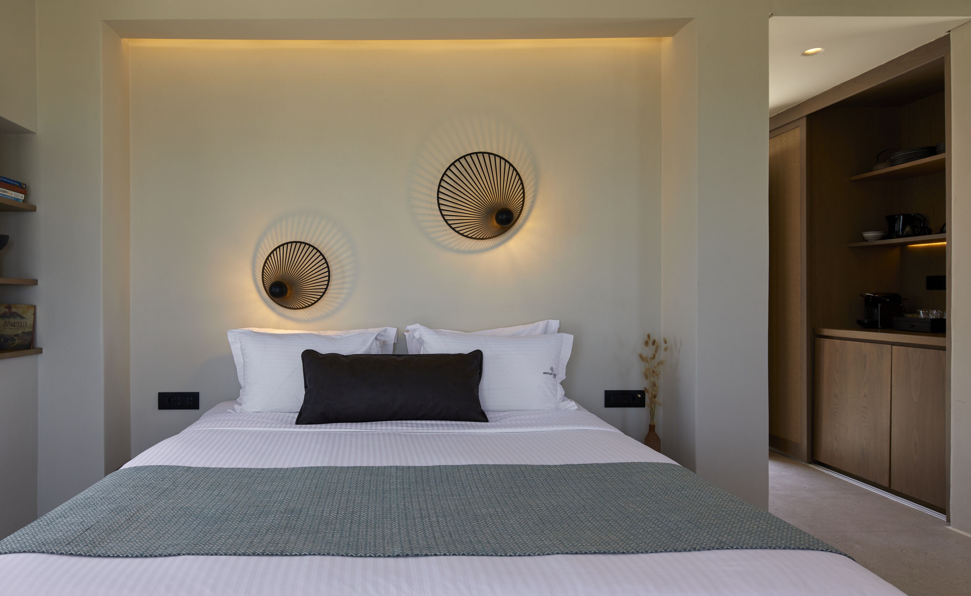 Quarto moderno com uma cama grande, duas luminárias fixadas na parede, um guarda-roupa de madeira e uma pequena planta.