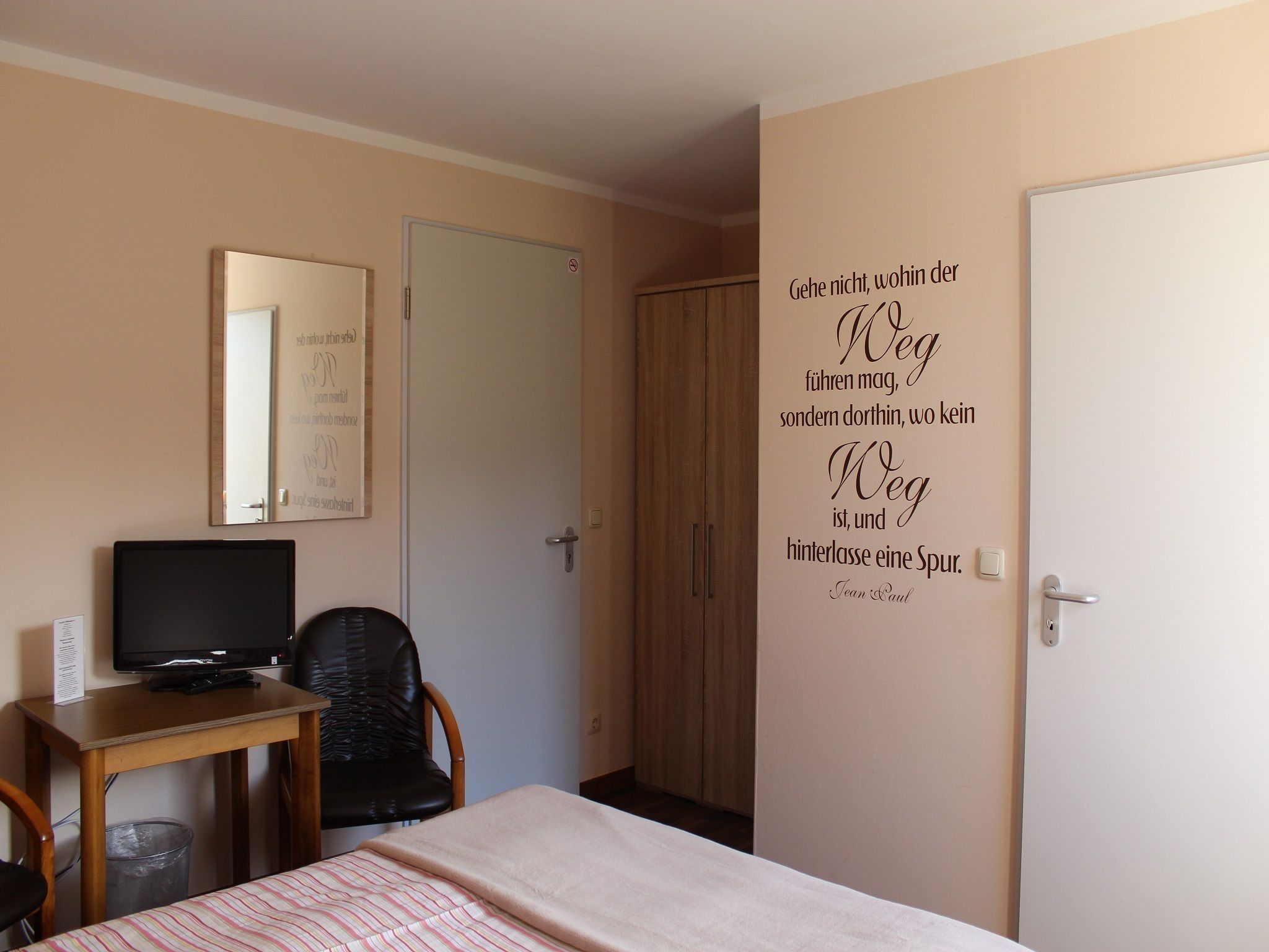 Quarto de hotel com uma cama, uma secretária com computador, uma cadeira e um guarda-roupa.