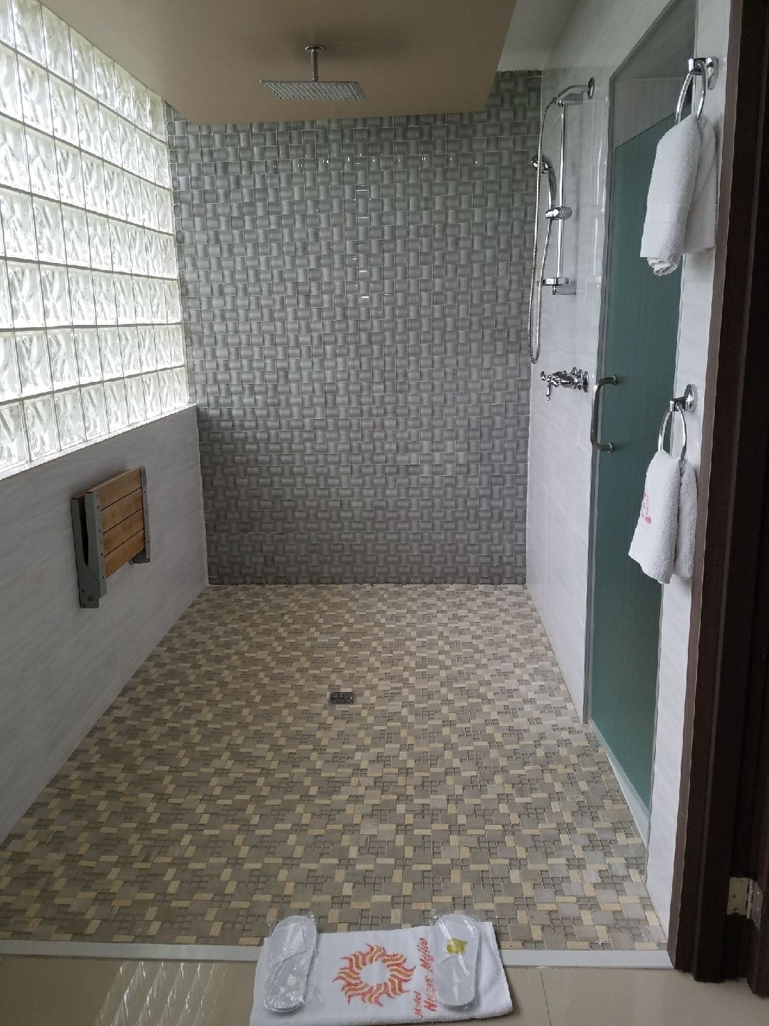 Área de chuveiro com piso ladrilhado, porta de vidro e porta-toalhas.