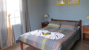 Cama bem arrumada com roupa de cama listrada e toalhas dobradas, abajur de cabeceira e janela com cortinas.
