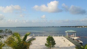 Uma praia com um gazebo, um píer com barcos e uma vista clara do mar.