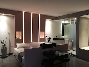 Quarto moderno com cama, mesa de cabeceira e escrivaninha com um laptop.