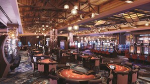 Um cassino com várias mesas de blackjack, máquinas caça-níqueis e um grande lustre.