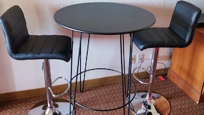 Uma mesa redonda pequena com duas cadeiras pretas, cada uma com base metálica.