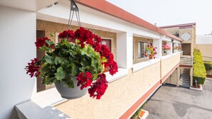 Um edifício com fachada bege, telhado vermelho e uma varanda com vasos de flores pendurados.