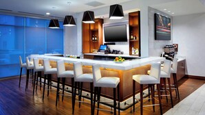 Cozinha moderna com ilha central, banquetas, uma grande TV de tela plana e armários de madeira.