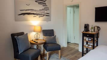Quarto de hotel com duas poltronas, uma mesinha de centro com abajur, cama, área de café e um quadro na parede.