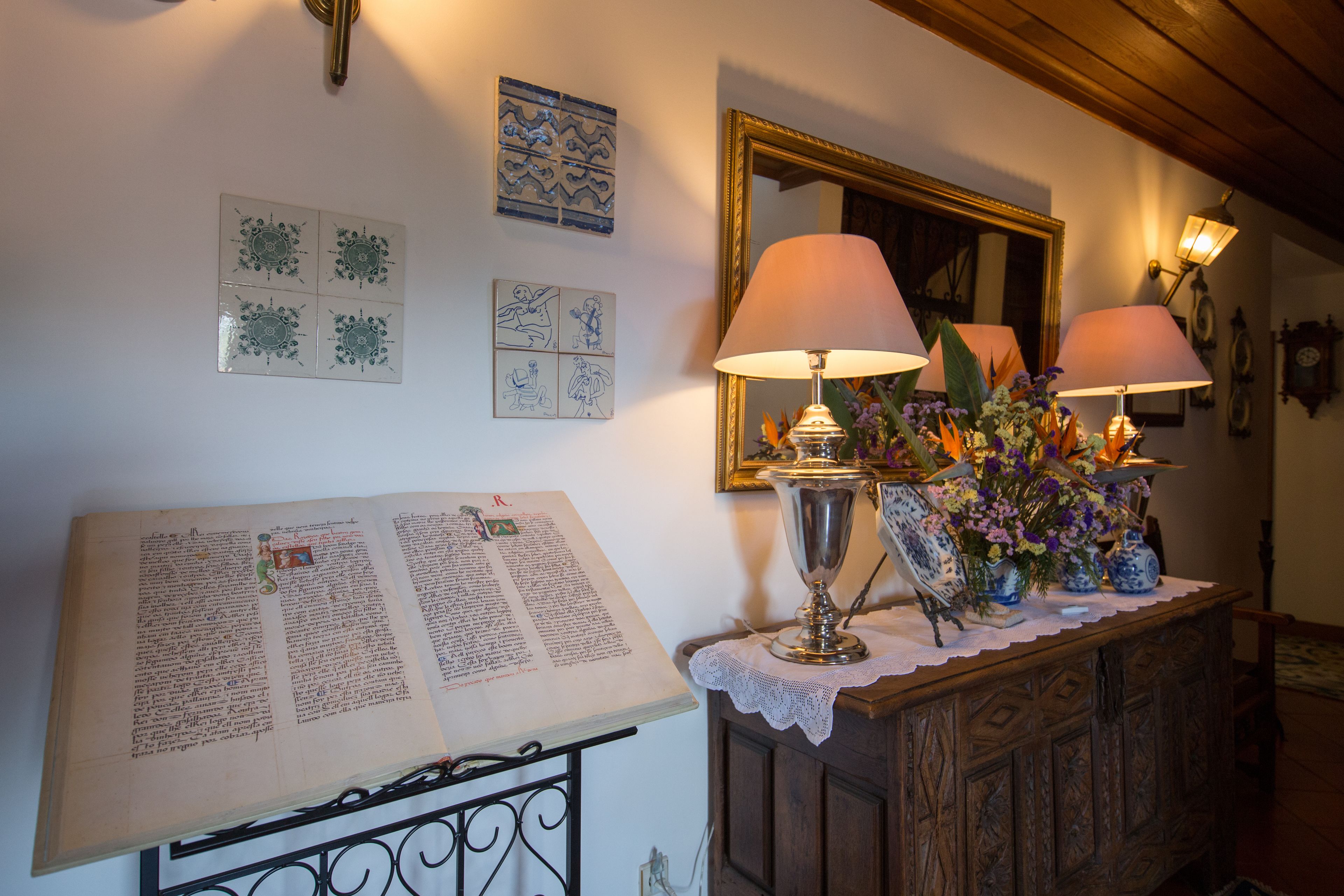 Quarto com uma mesa exibindo um livro, duas luminárias, um espelho e decorações na parede.