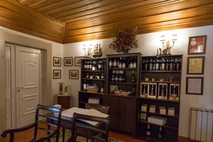 Uma sala de jantar com teto de madeira, uma mesa com cadeiras e prateleiras com garrafas de vinho e certificados emoldurados.