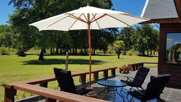 Um pátio externo com bancos de madeira, uma mesa redonda e um grande guarda-sol.