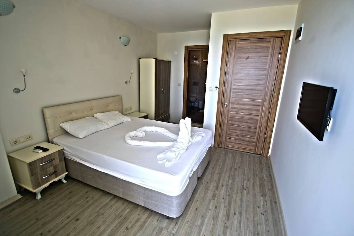 Uma cama bem arrumada com uma toalha, uma mesa de cabeceira com um controle remoto e um guarda-roupa em um quarto de hotel.