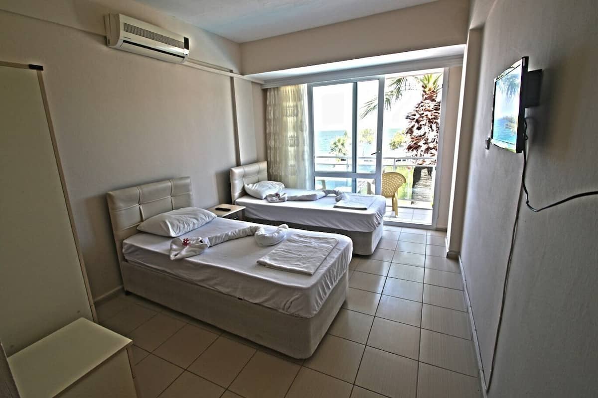 Quarto de hotel com duas camas, uma varanda e vista para o mar, e uma televisão presa à parede.