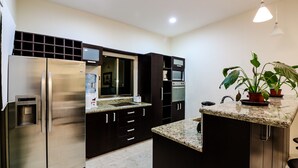Cozinha moderna com eletrodomésticos de aço inoxidável, armários escuros, bancadas de granito e um vaso com planta.
