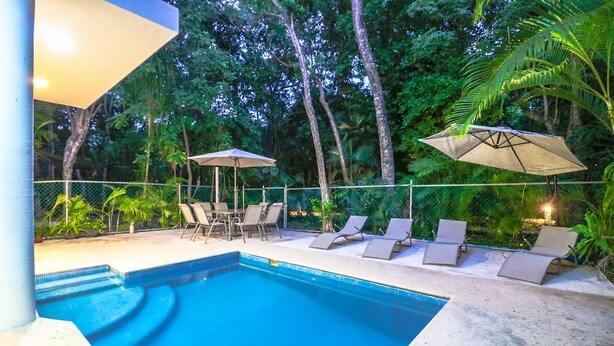 Piscina com espreguiçadeiras e guarda-sóis, rodeada por uma cerca e vegetação exuberante.