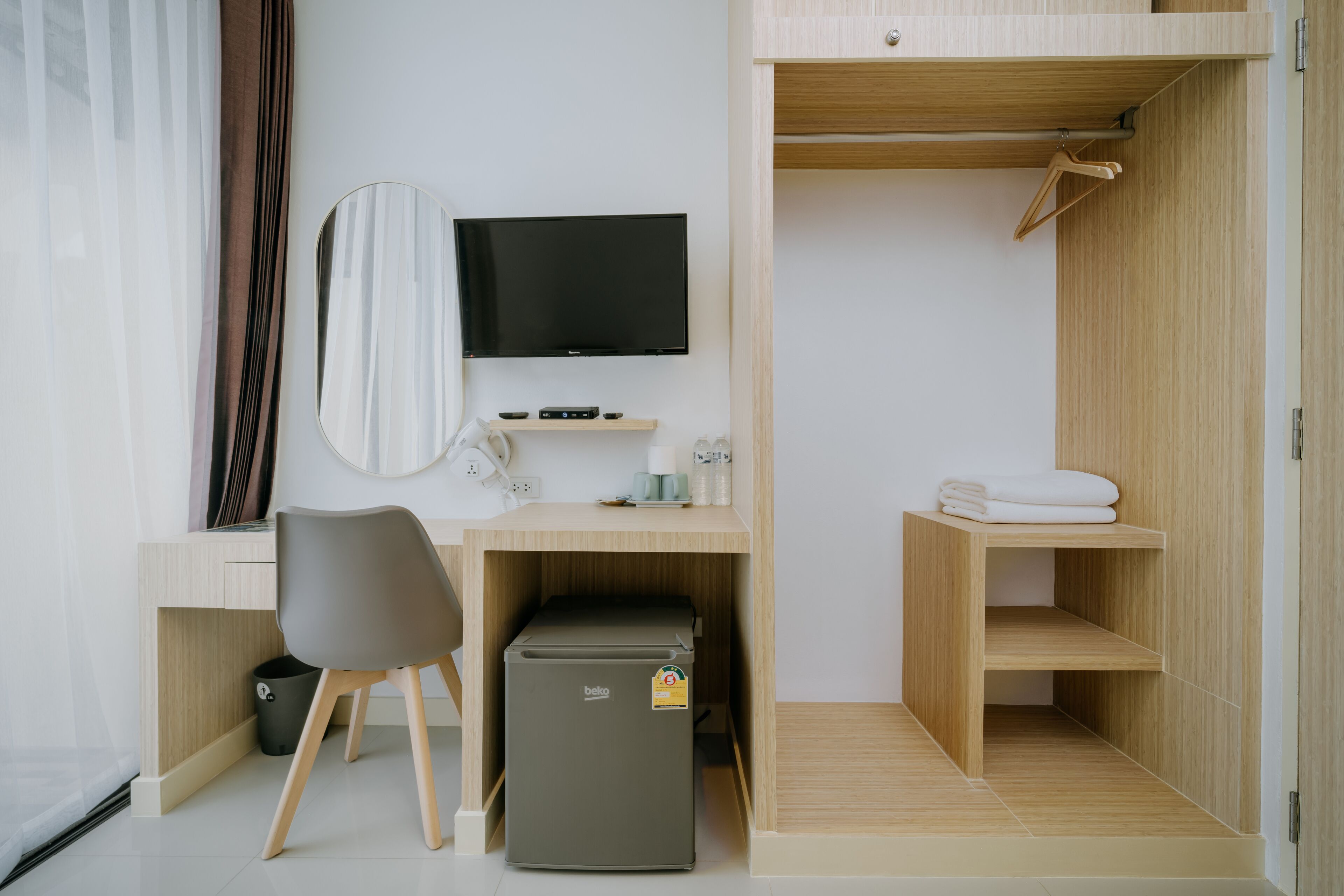 Quarto de hotel compacto com escrivaninha, cadeira, televisão e um pequeno frigorífico.