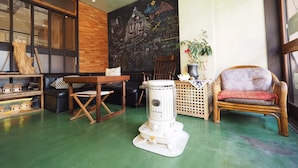 Um quarto aconchegante com piso de madeira, um quadro negro com desenhos, um aquecedor branco, uma mesa de madeira, um sofá de couro preto e uma cadeira de vime.
