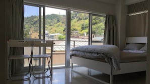 Quarto com cama, uma cadeira e grandes janelas com vista para uma paisagem verde.
