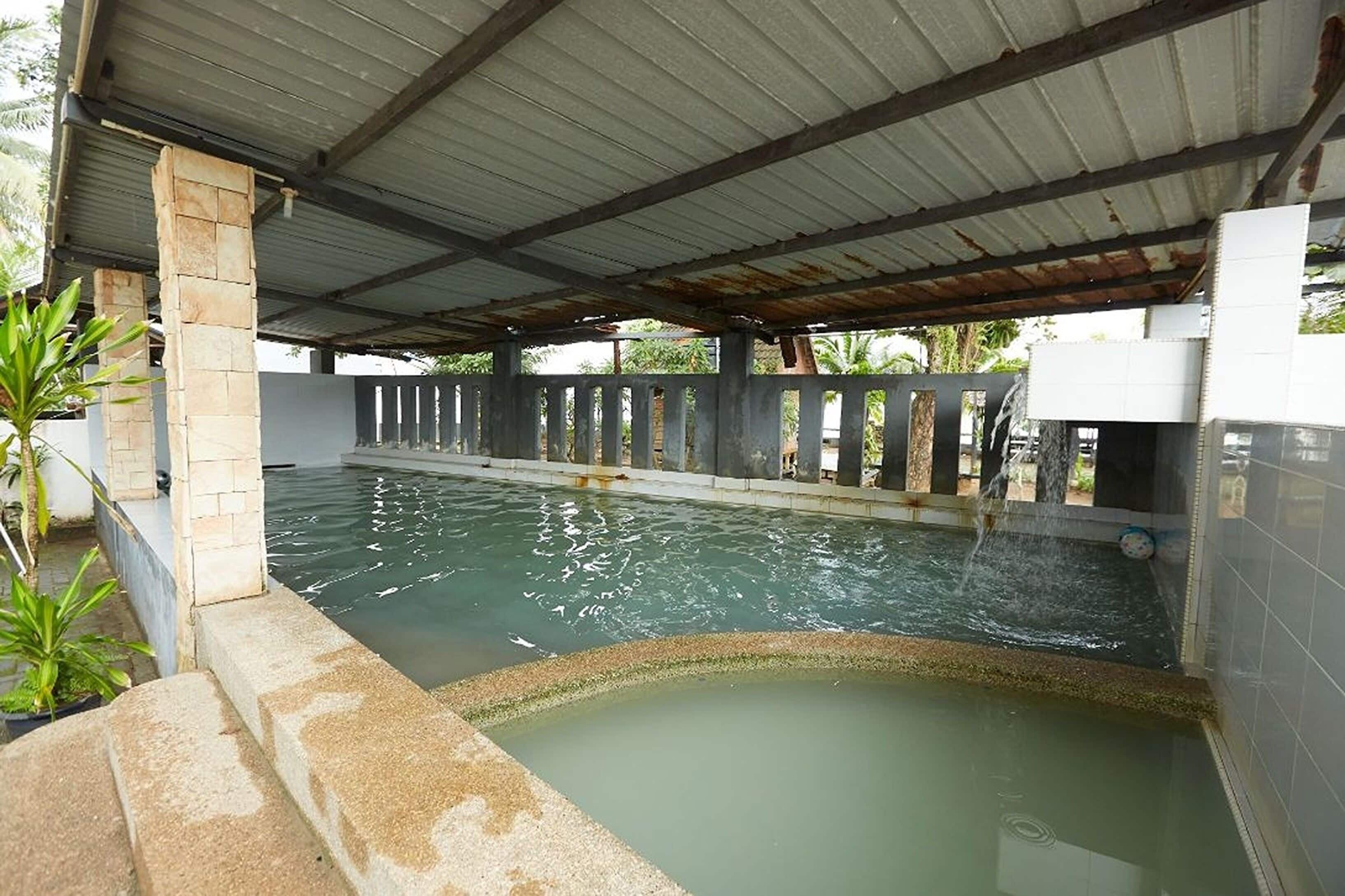 Piscina coberta com parede de pedra e cobertura metálica.