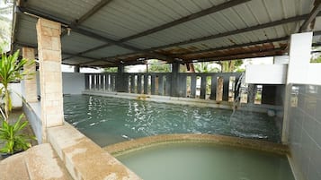 Piscina coberta com parede de pedra e cobertura metálica.